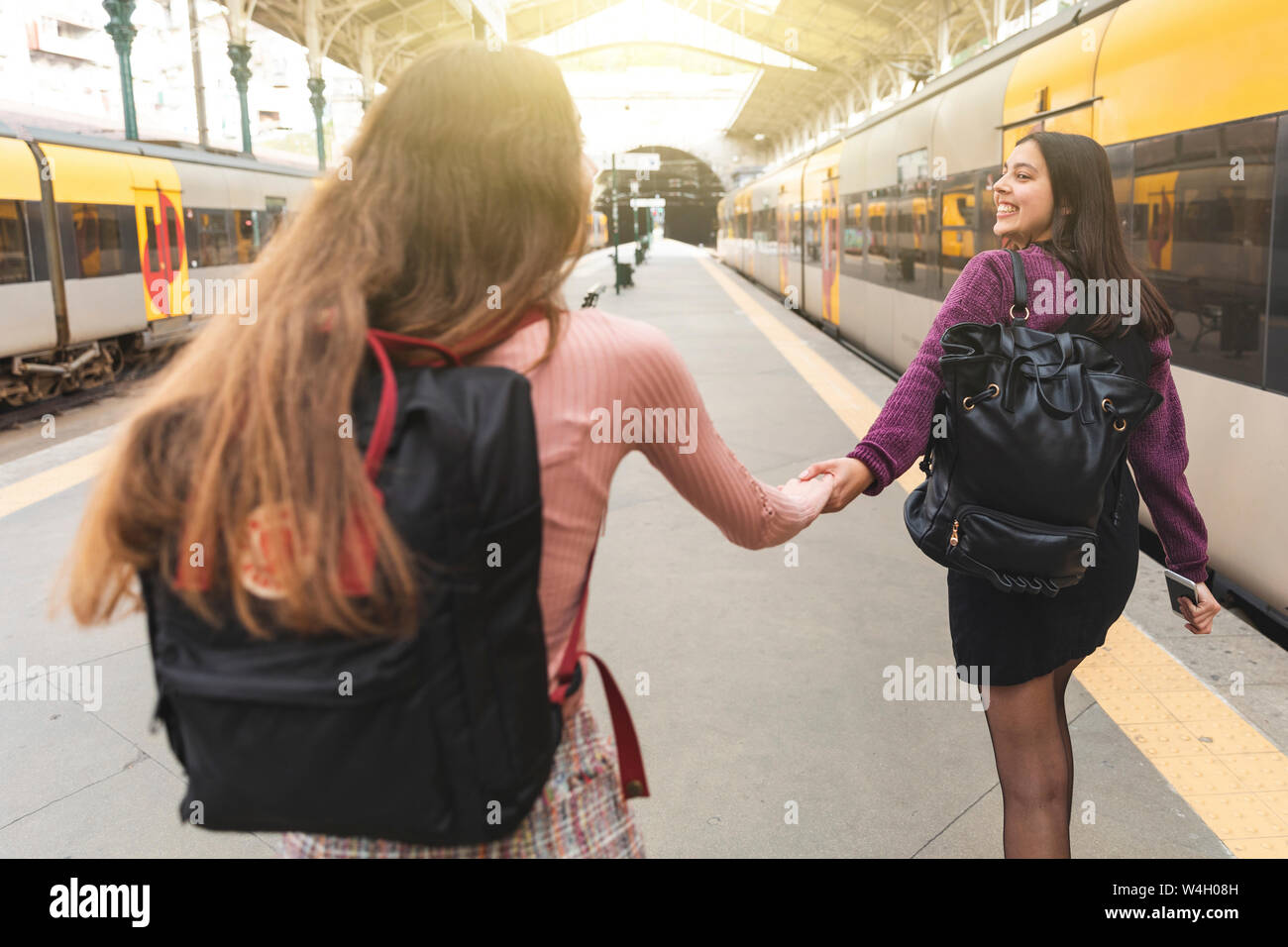 Back view of two young women with backpacks hand in hand on platform ...