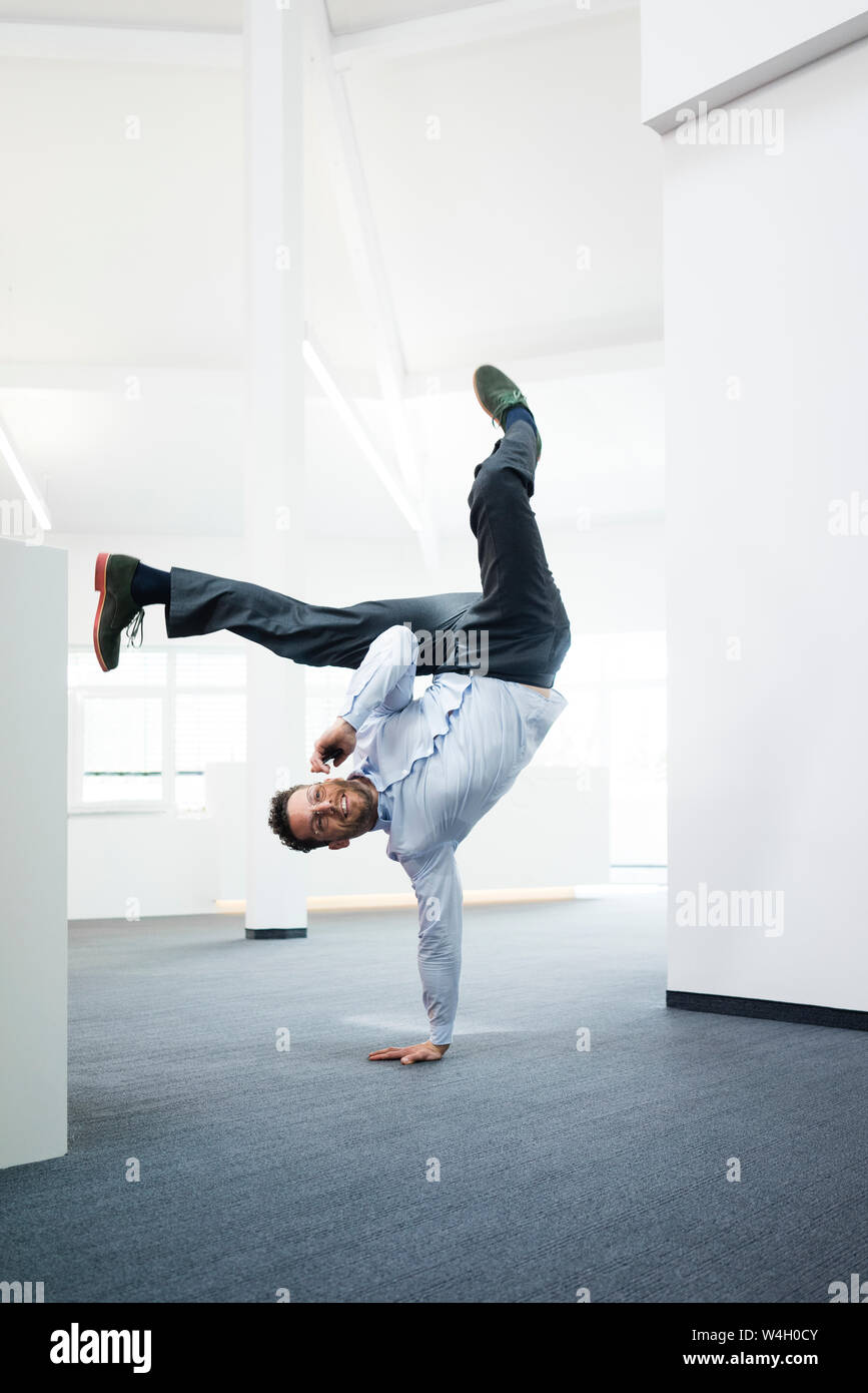 Businessman with cell phone doing a one-handed handstand on office ...
