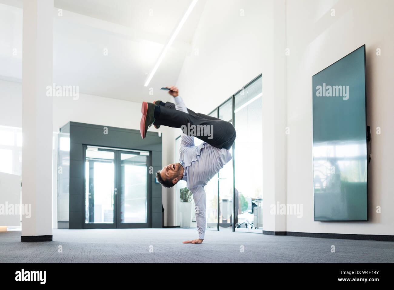 Businessman with cell phone doing a one-handed handstand on office ...