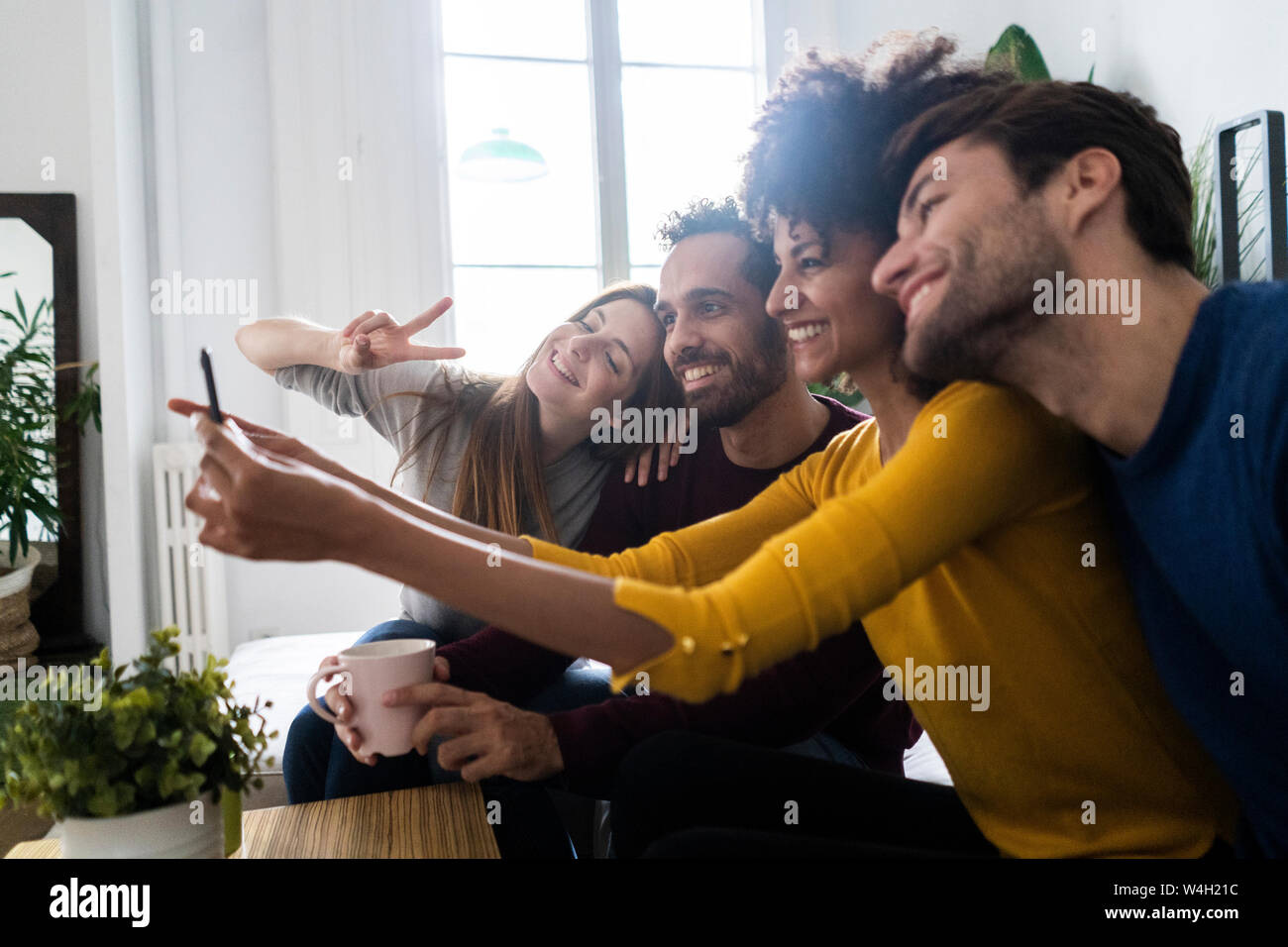 Four happy friends sitting on couch taking a selfie Stock Photo - Alamy