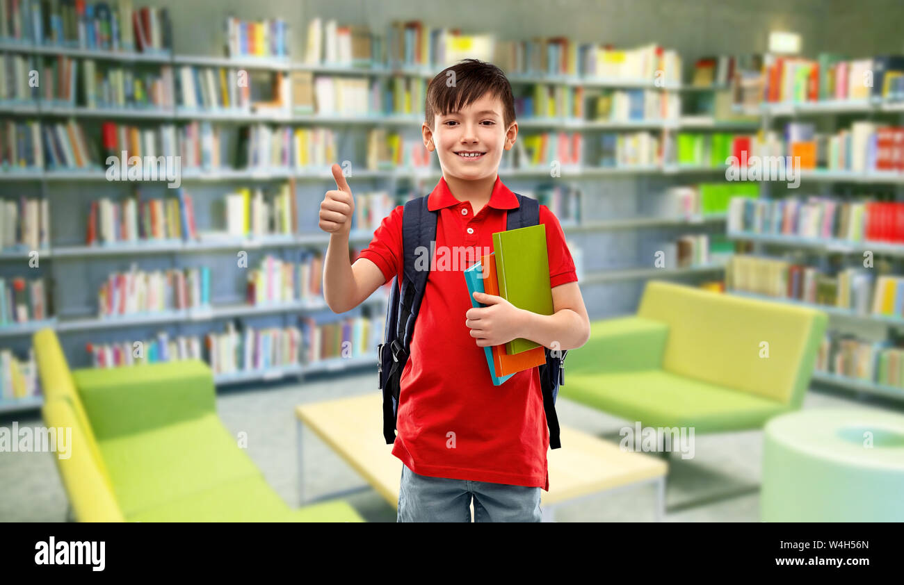 schoolboy with books showing thumbs up at library Stock Photo - Alamy