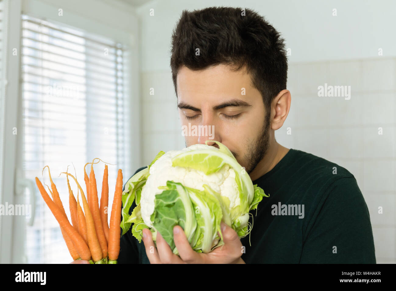 Young handsome brunette man holding fresh vegetables in his hands. With ...