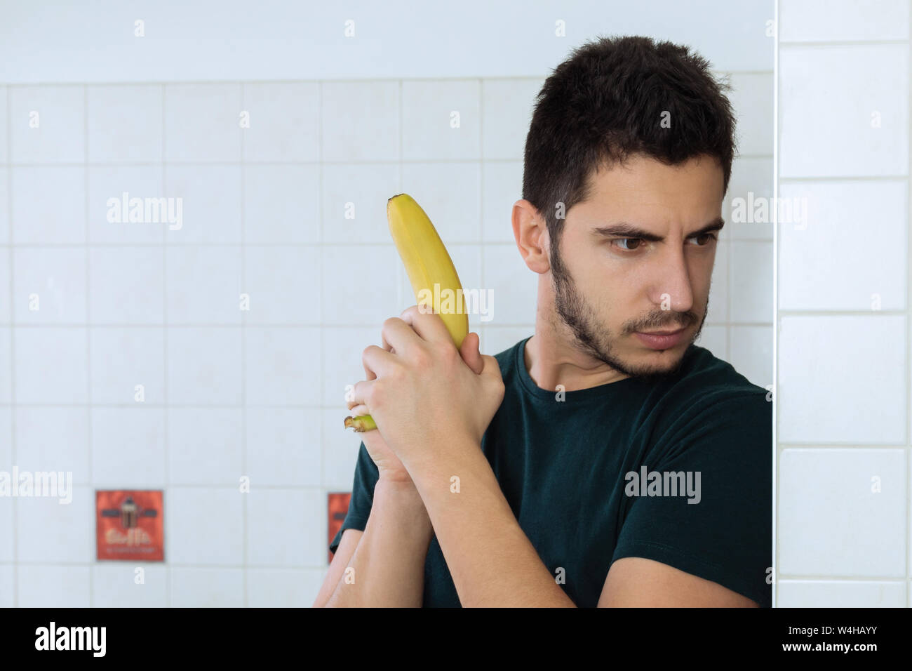 Young handsome man having fun in his kitchen imagining that a banana is ...