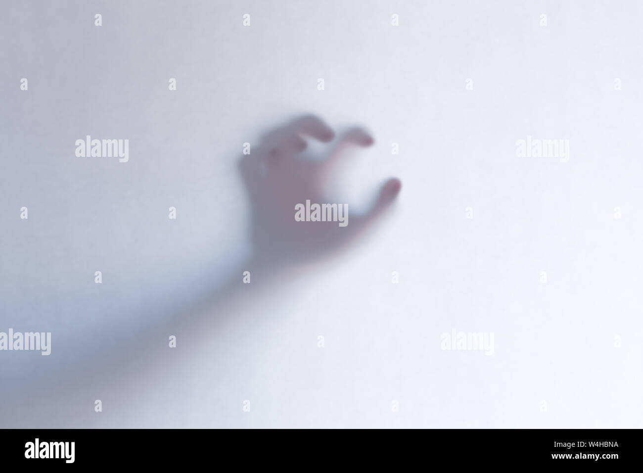 Blurred scary ghost hands behind a white glass background. Horizontal ...