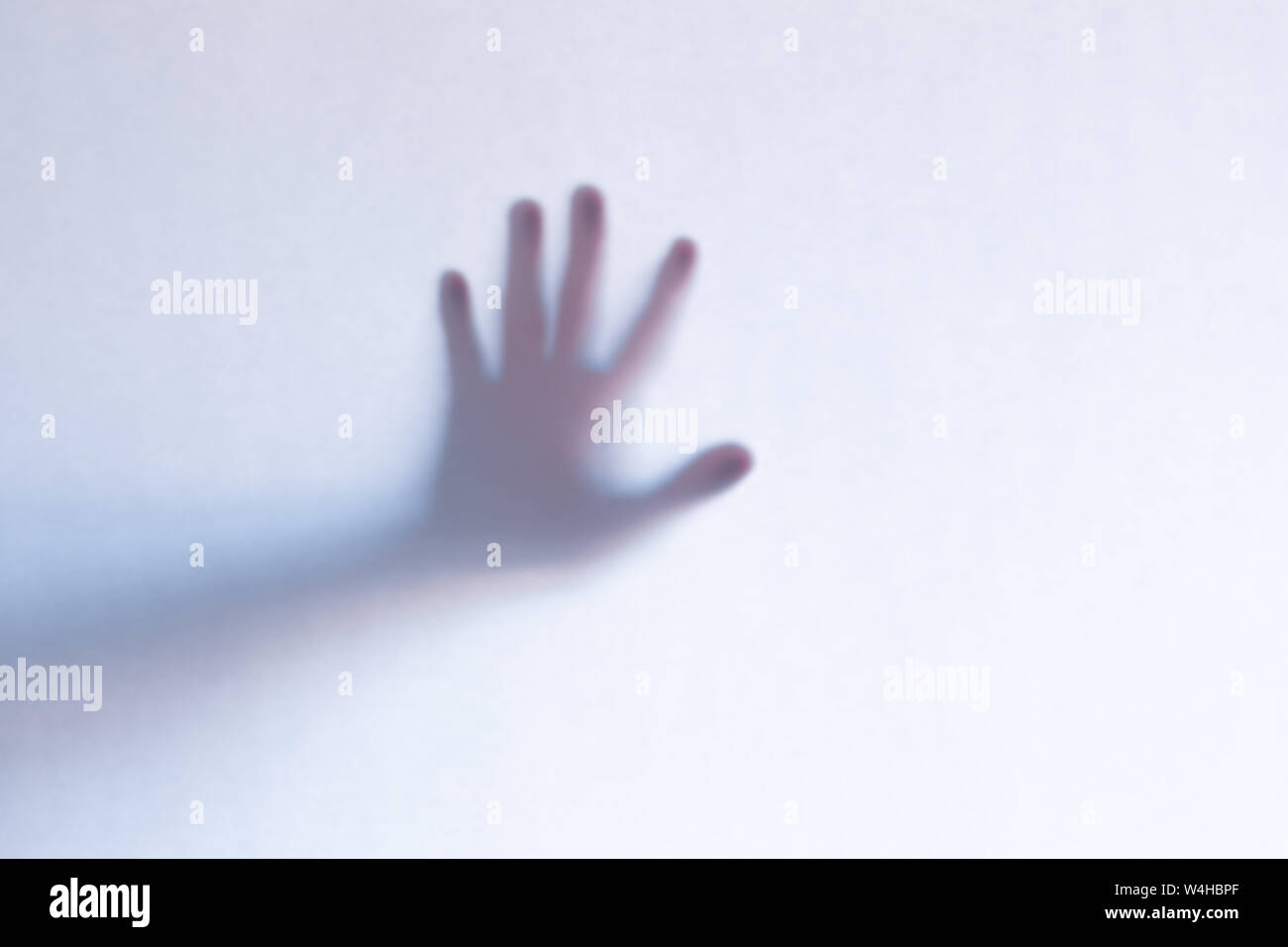 Blurred scary ghost hands behind a white glass background. Horizontal ...
