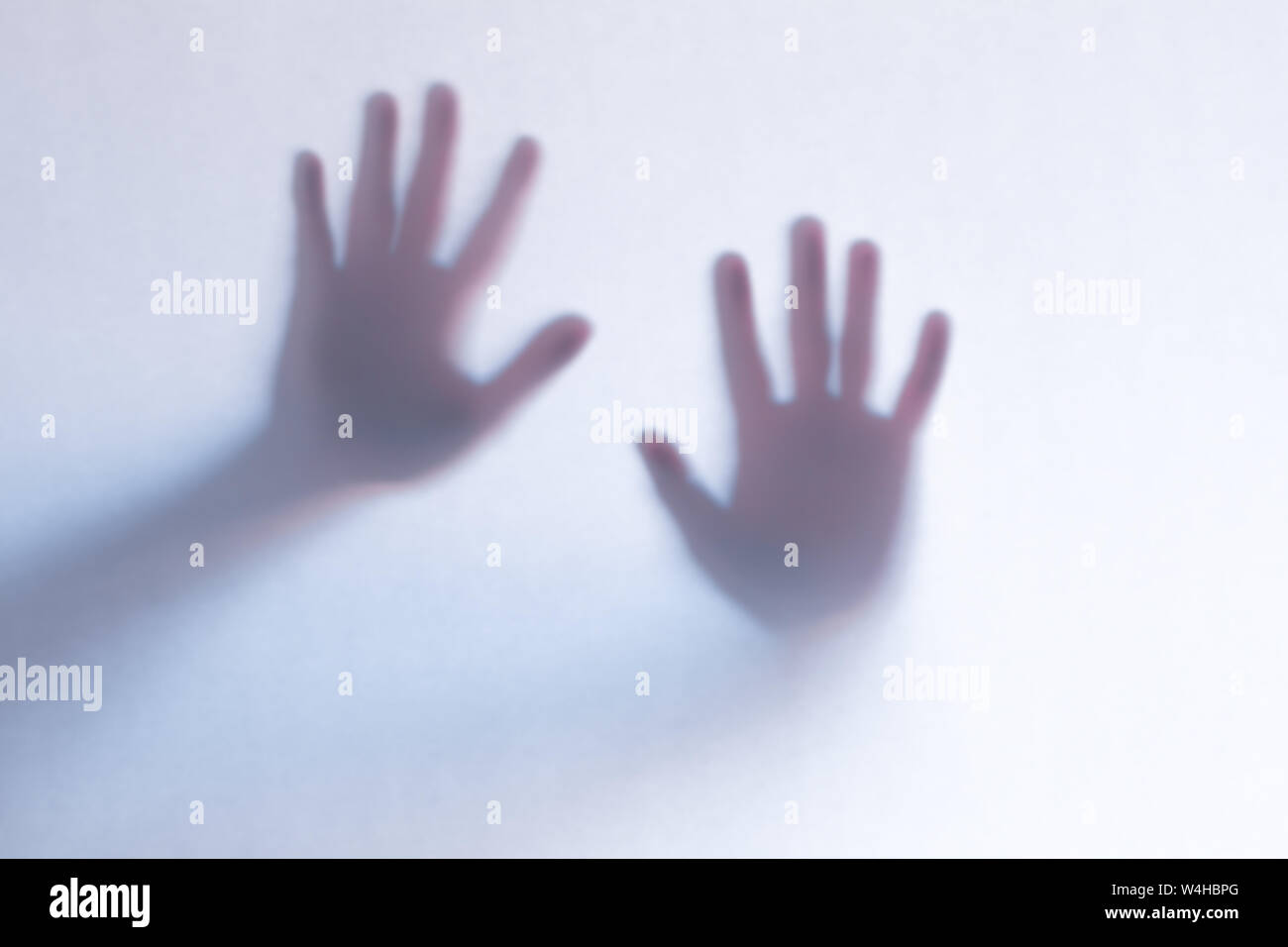 Blurred scary ghost hands behind a white glass background. Horizontal ...