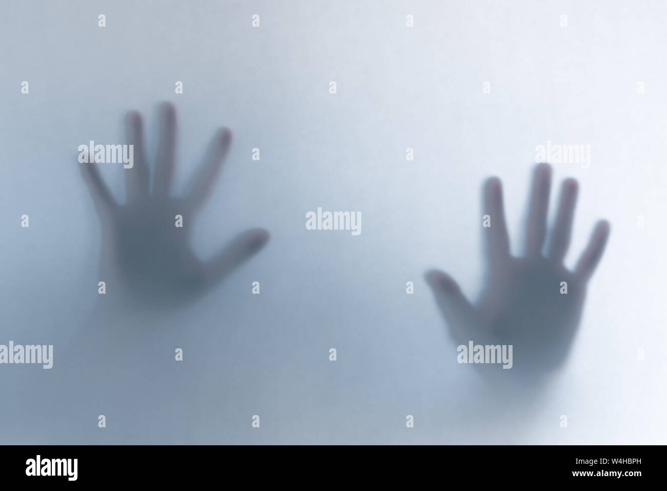 Blurred scary ghost hands behind a white glass background. Horizontal ...
