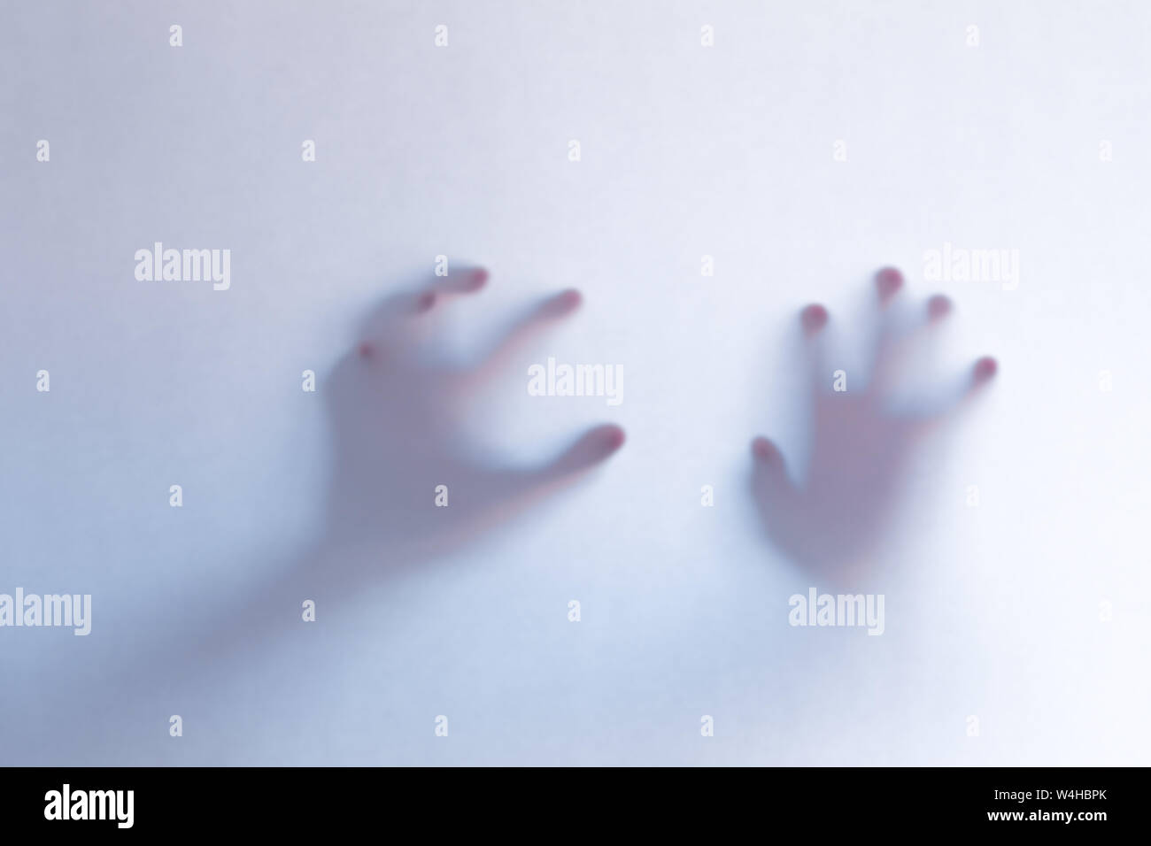 Blurred scary ghost hands behind a white glass background. Horizontal ...