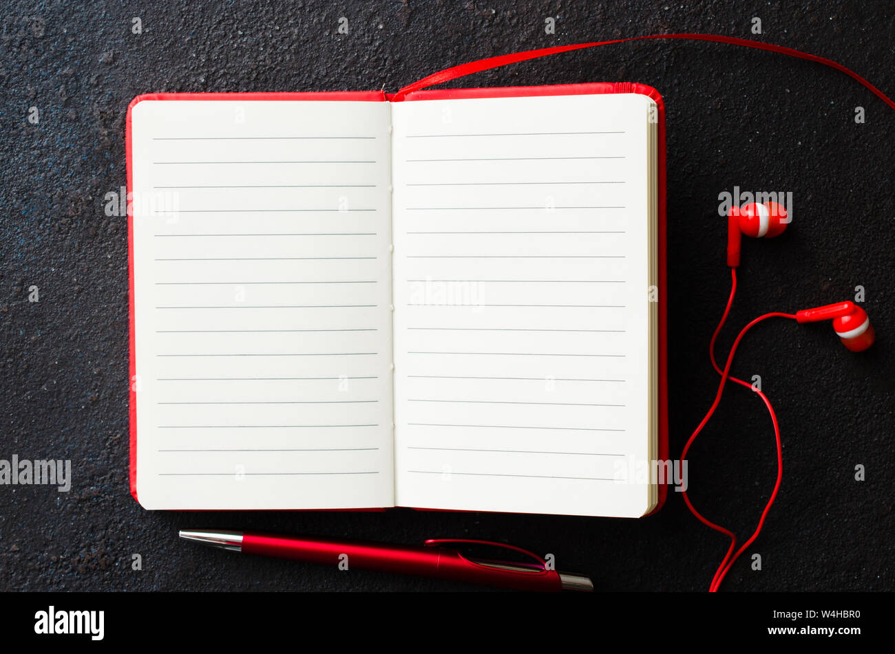 Empty red notebook with red pen and headphones on dark background ...