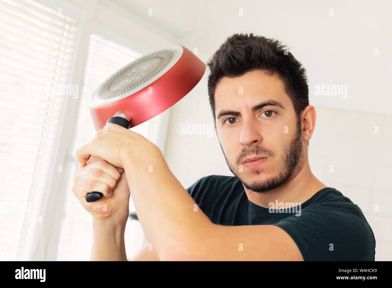 Crazy very angry young man threatening with frying pan on the kitchen ...
