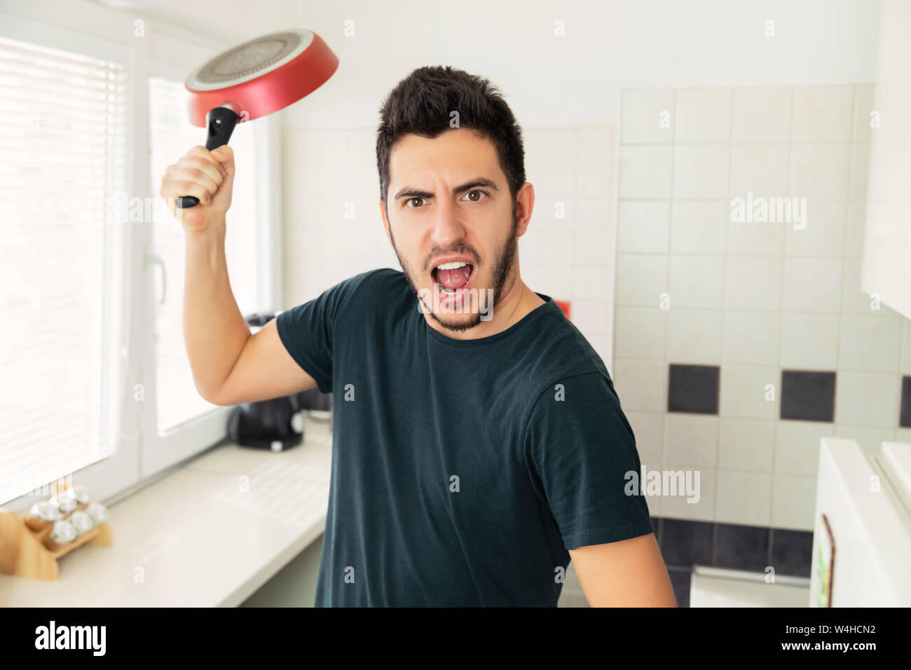 Crazy very angry young man threatening with frying pan on the kitchen ...