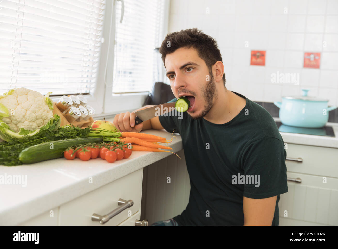 A young handsome man sits in the kitchen and reluctantly eats ...