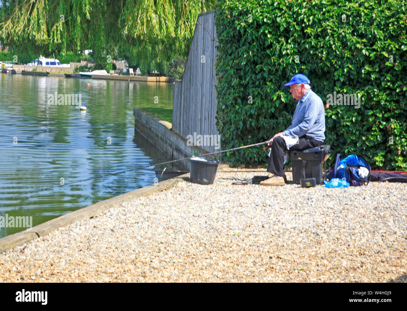 An elderly angler fishing from a small quay at South Walsham Broad on ...