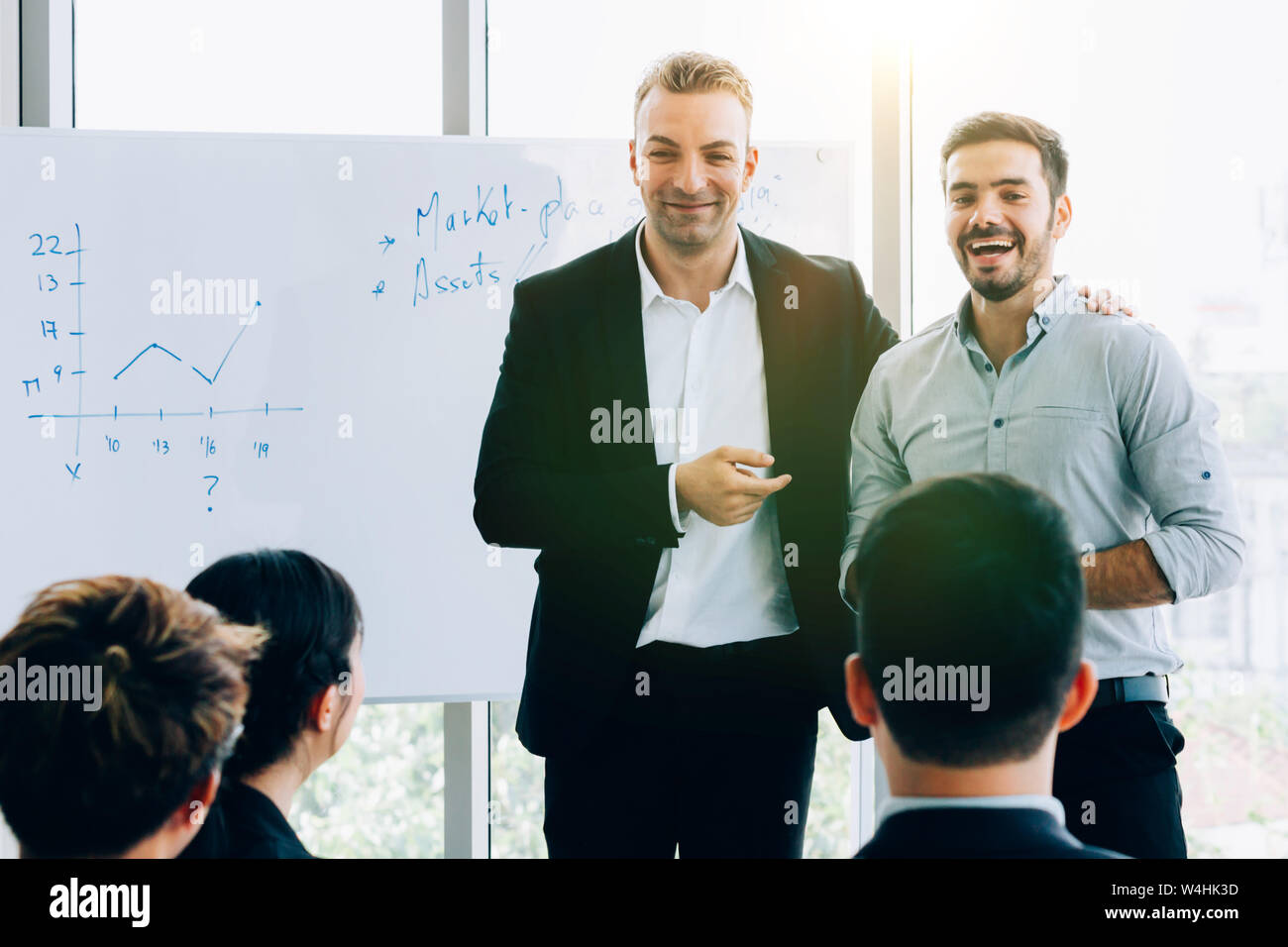 Smiling adult men in formal suits standing near whiteboard doing ...