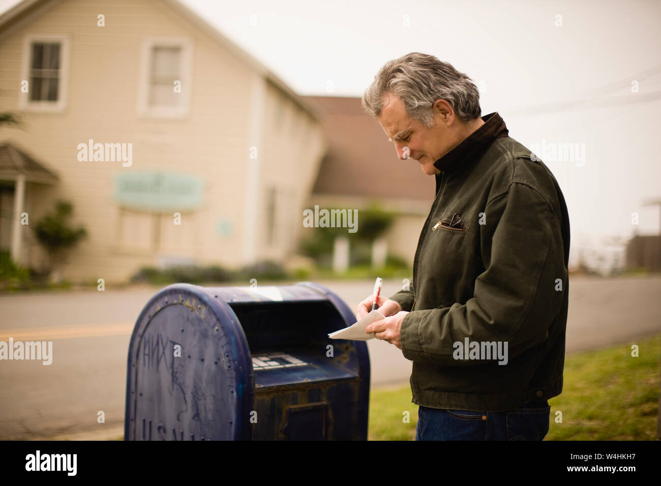 Man writing on letter next to post box Stock Photo - Alamy