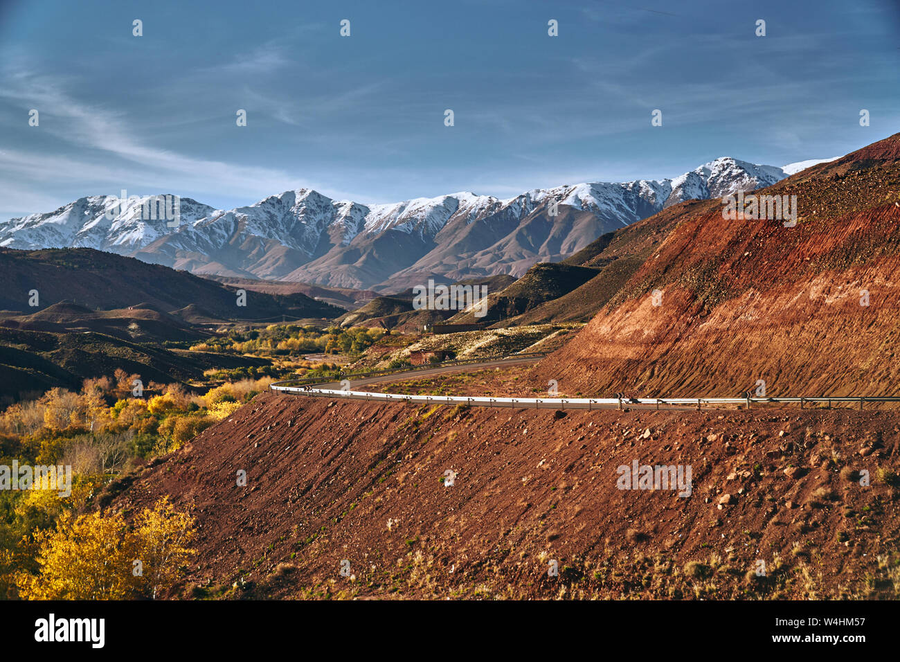 Curved road crossing red moroccan soil with snow covered Atlas ...
