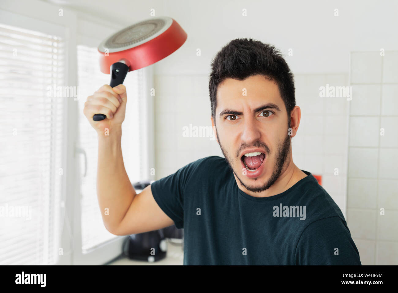 Crazy very angry young man threatening with frying pan on the kitchen ...