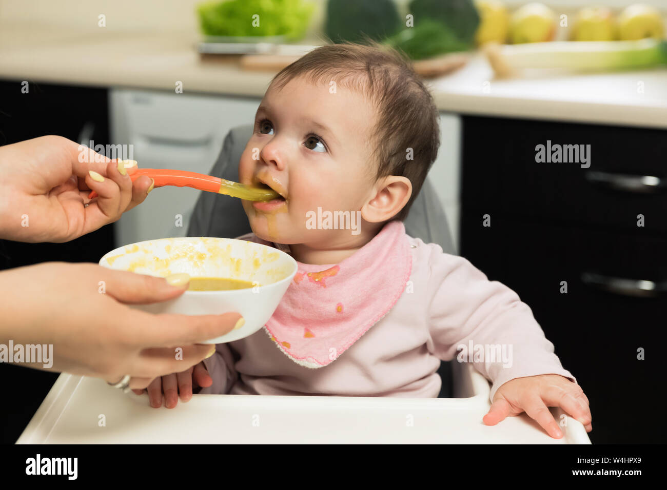Feeding. Adorable baby child eating with a spoon in a children's chair ...