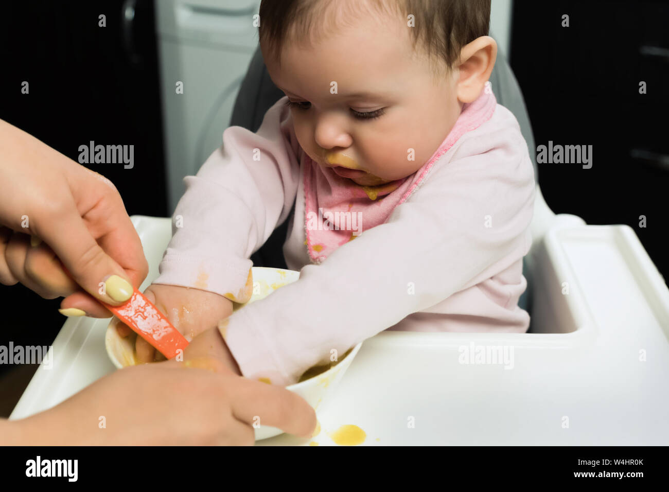 Feeding. Adorable baby child eating with a spoon in a children's chair ...