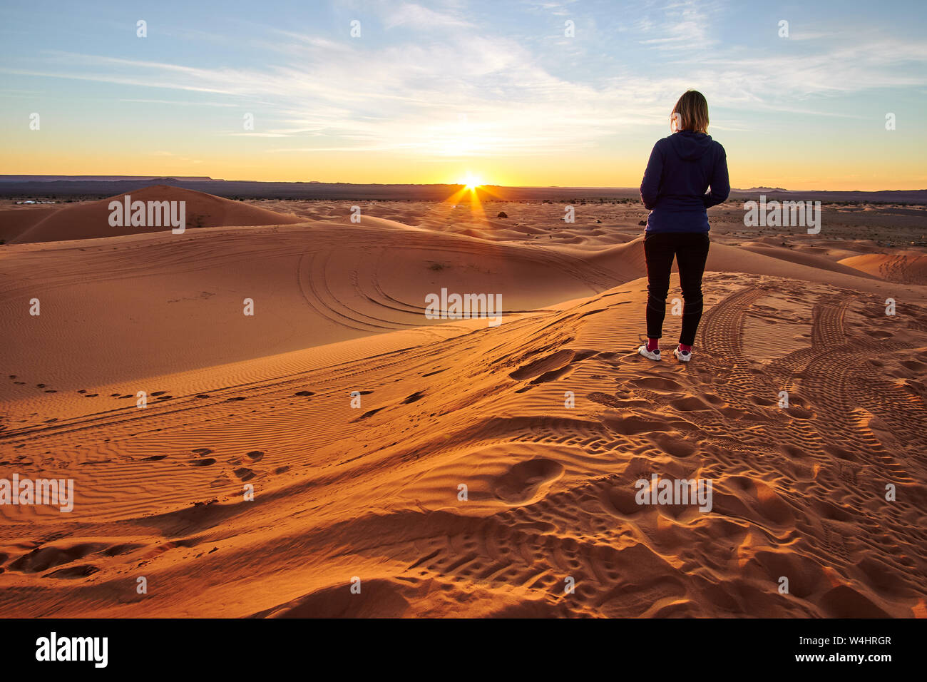 Blonde tourist girl watching sunrise in Sahara desert on top of the ...