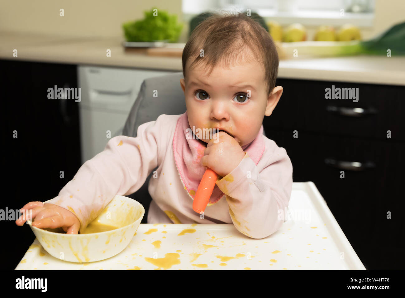 Feeding. Adorable baby child eating with a spoon in a children's chair ...