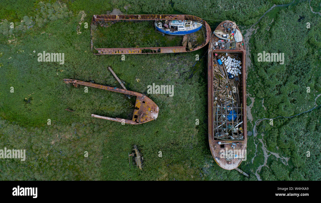 Shipwrecked and rusting barges sinking into the mud of a river estuary ...