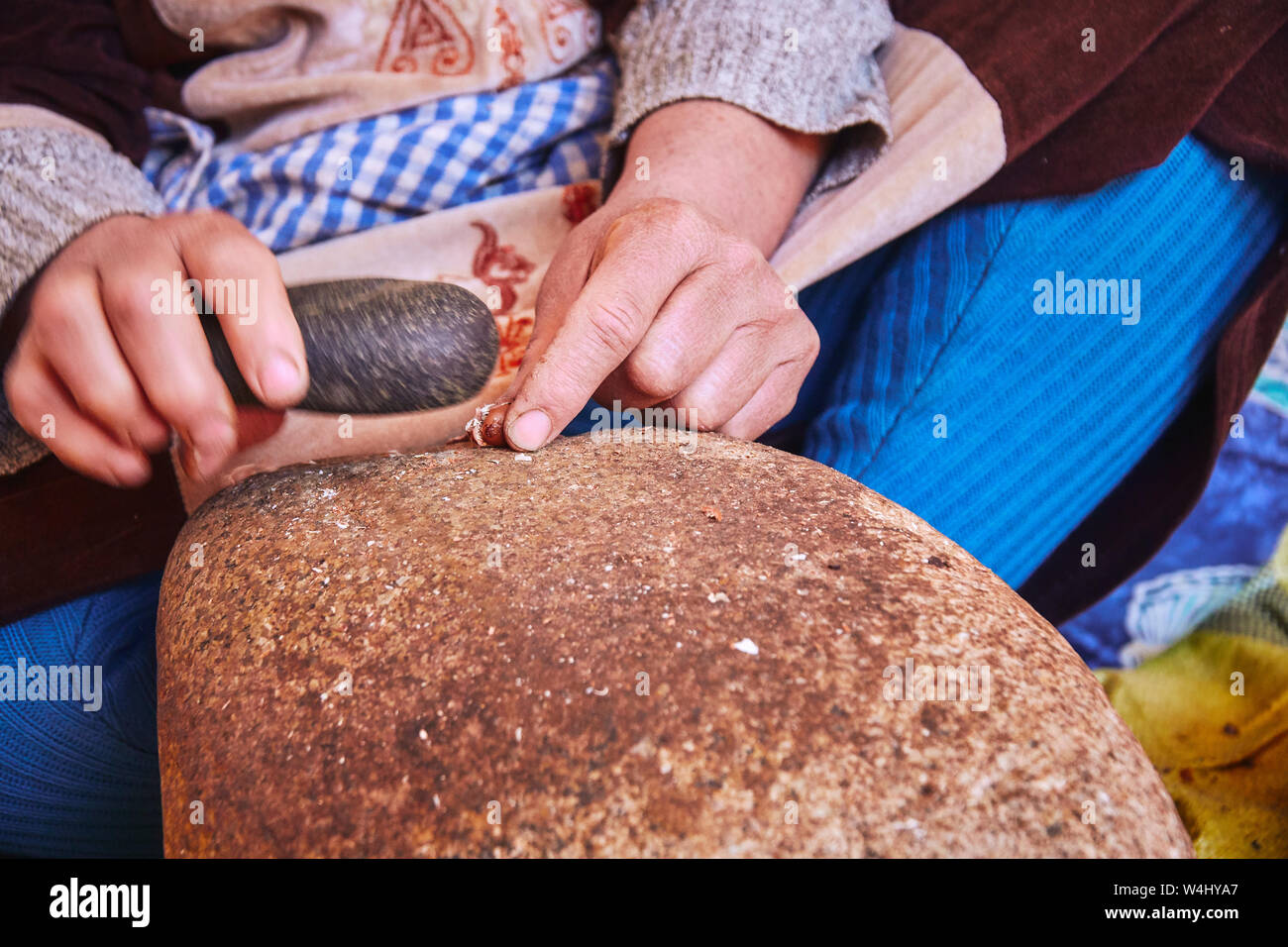 A moroccan woman cracking argan nuts with a stone tool on the stone to ...