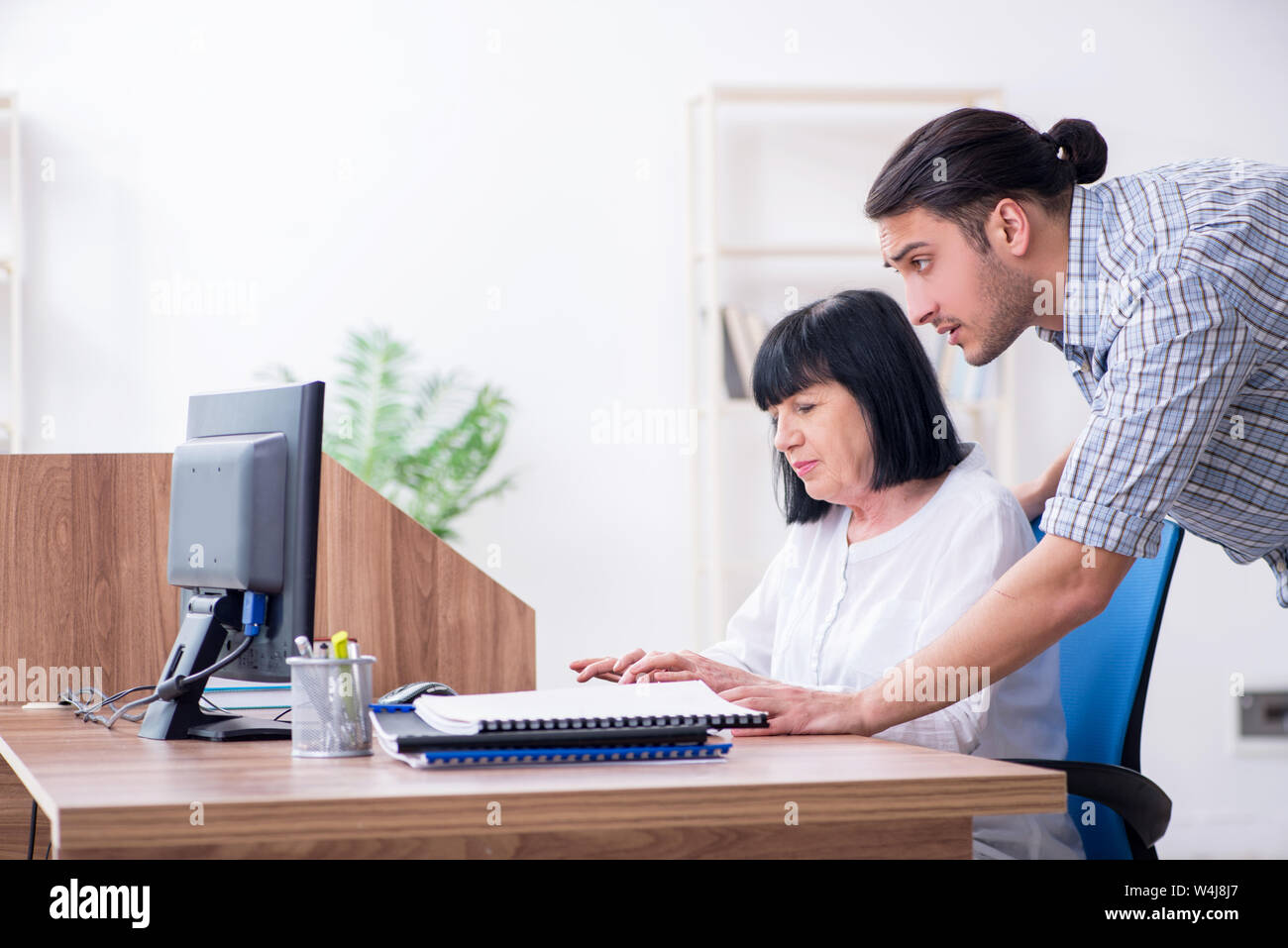 Young male employee explaining to old female colleague how to use ...