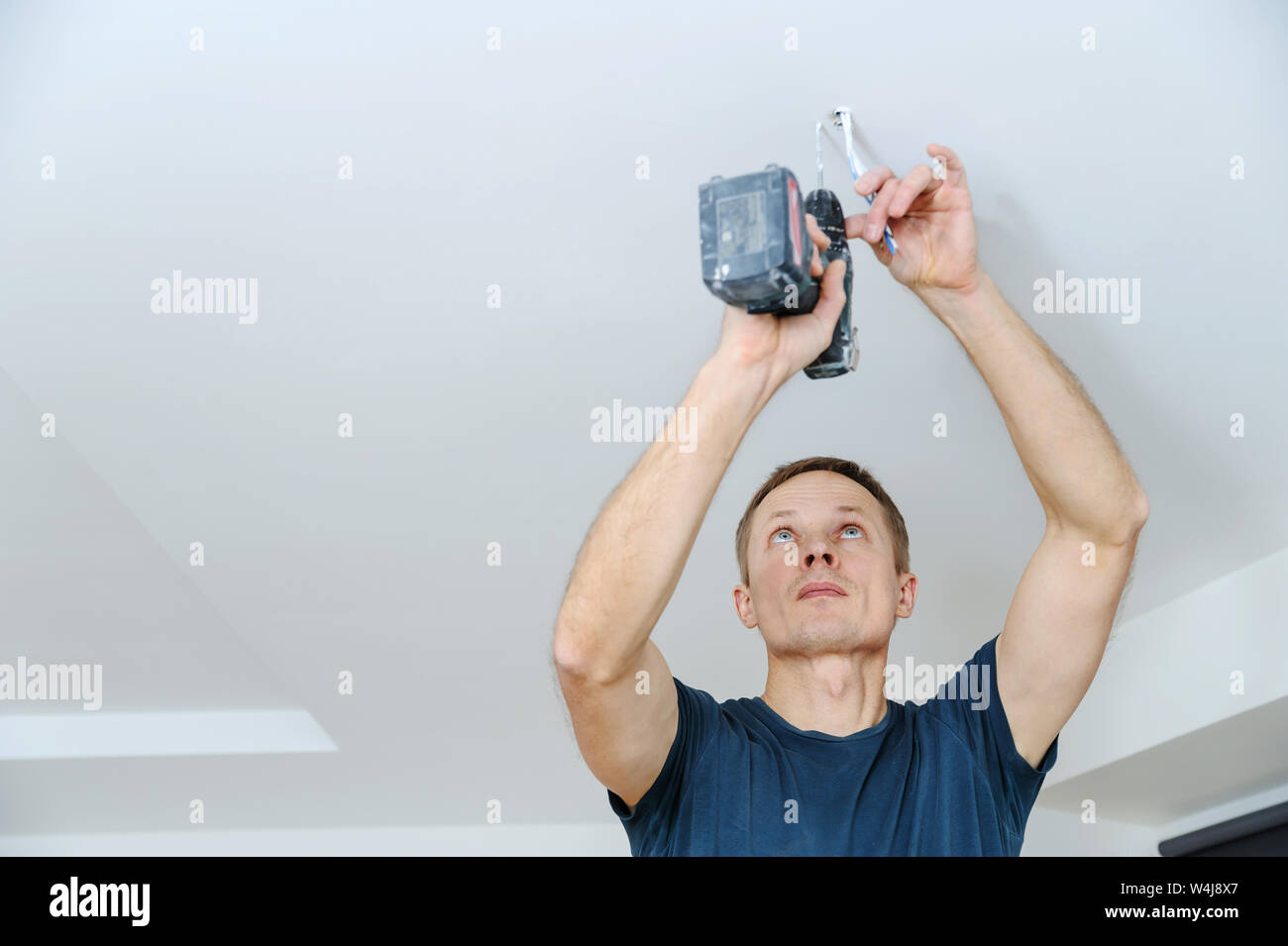 Installing a spotlight in the room. The man is drilling the ceiling to ...