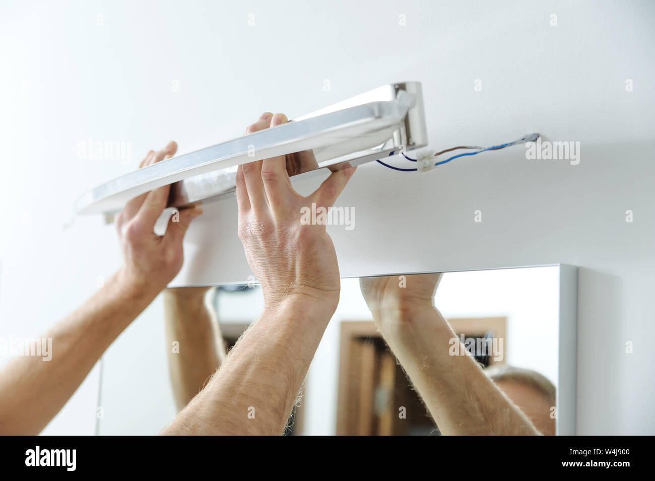Installing a lamp at home. The man is fixing the lamp on the wall above ...