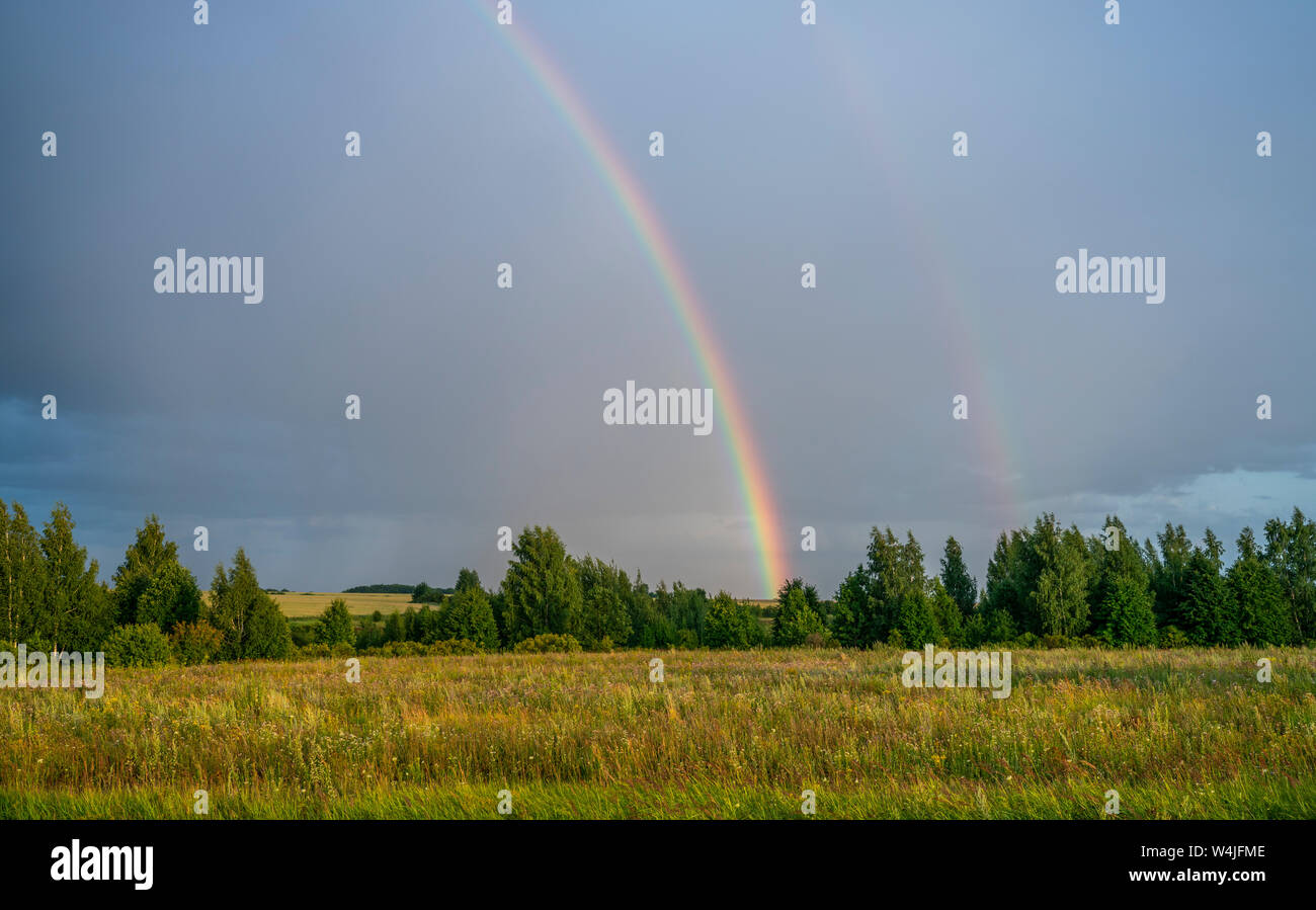 rain and rainbow over fields and tree planting Stock Photo - Alamy