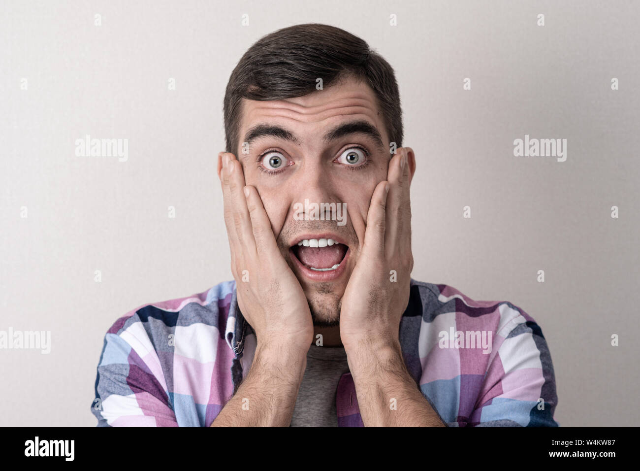 Close-up portrait of young Caucasian man with shocked face holding his ...