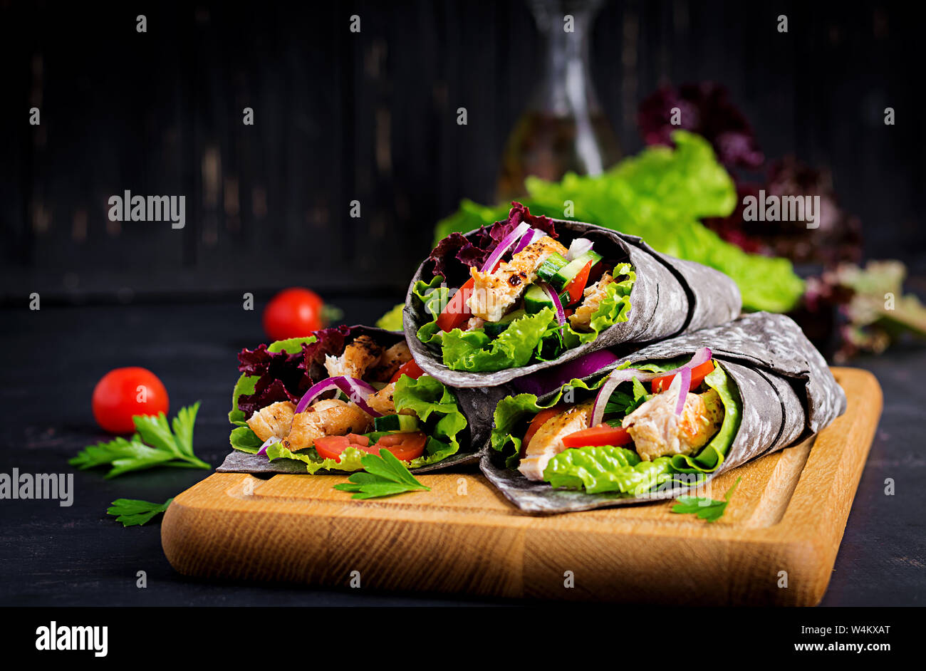 Tortilla with added ink cuttlefish wraps with chicken and vegetables on black background ...
