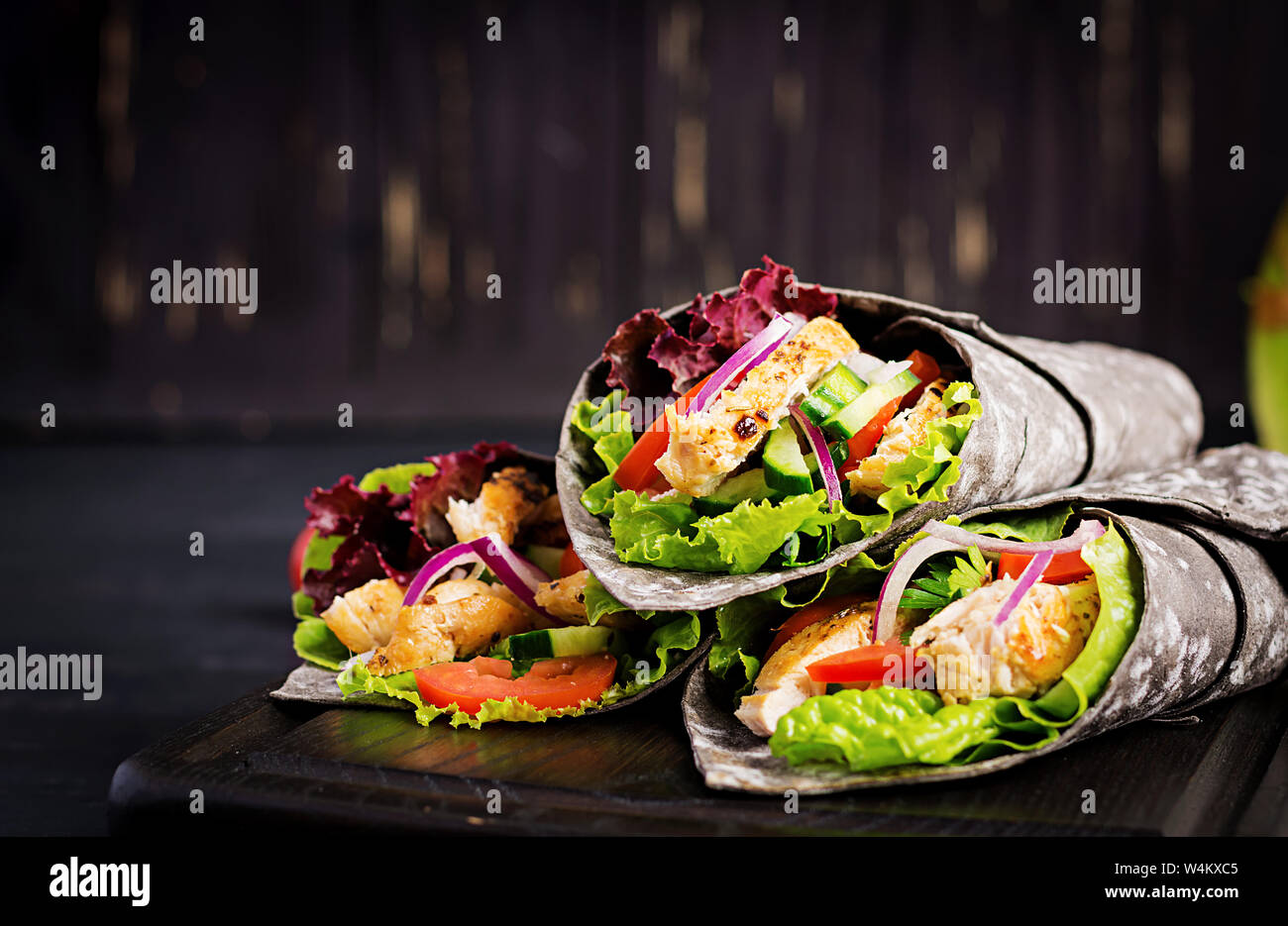 Tortilla with added ink cuttlefish wraps with chicken and vegetables on black background ...