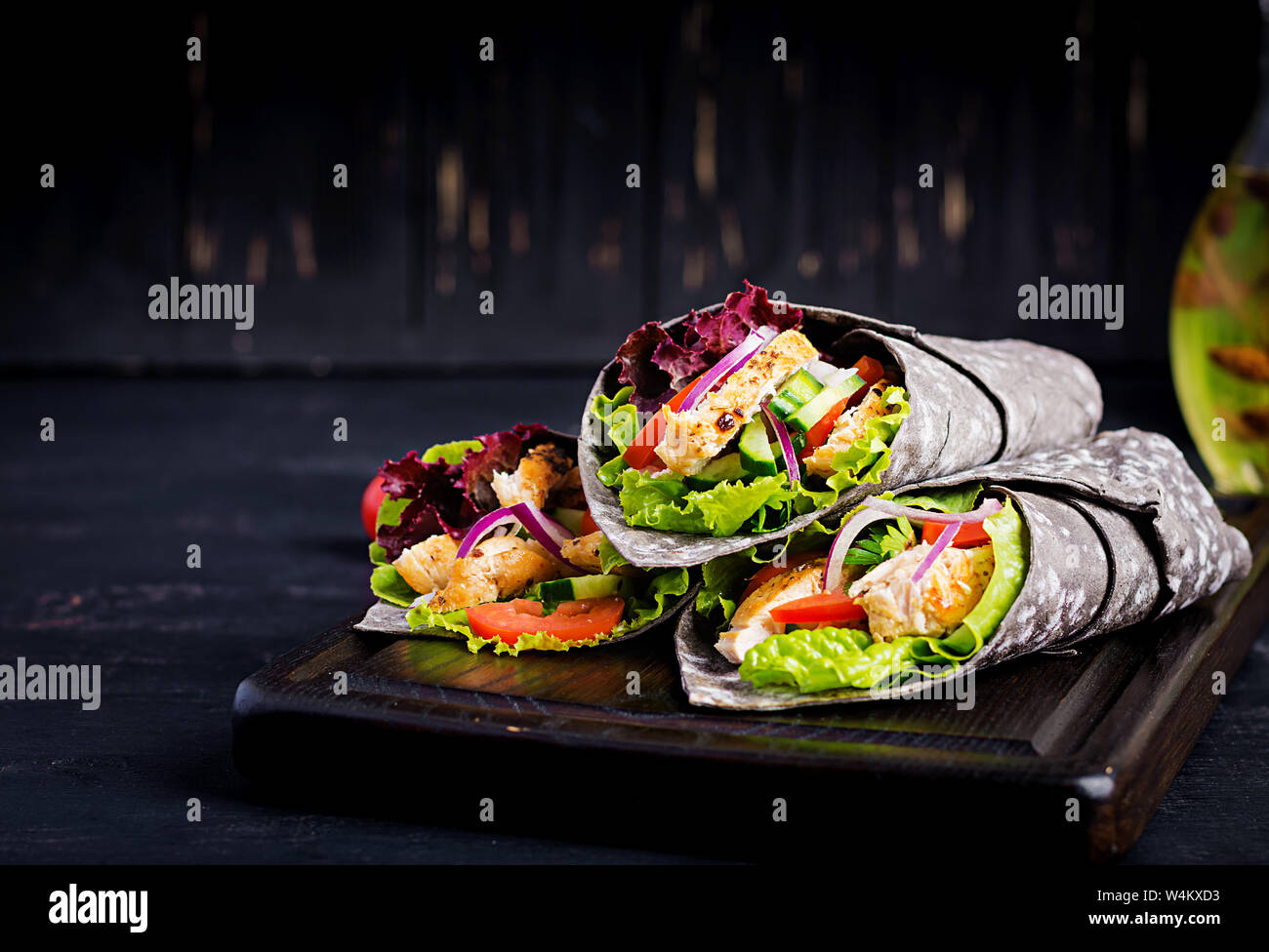 Tortilla with added ink cuttlefish wraps with chicken and vegetables on black background ...