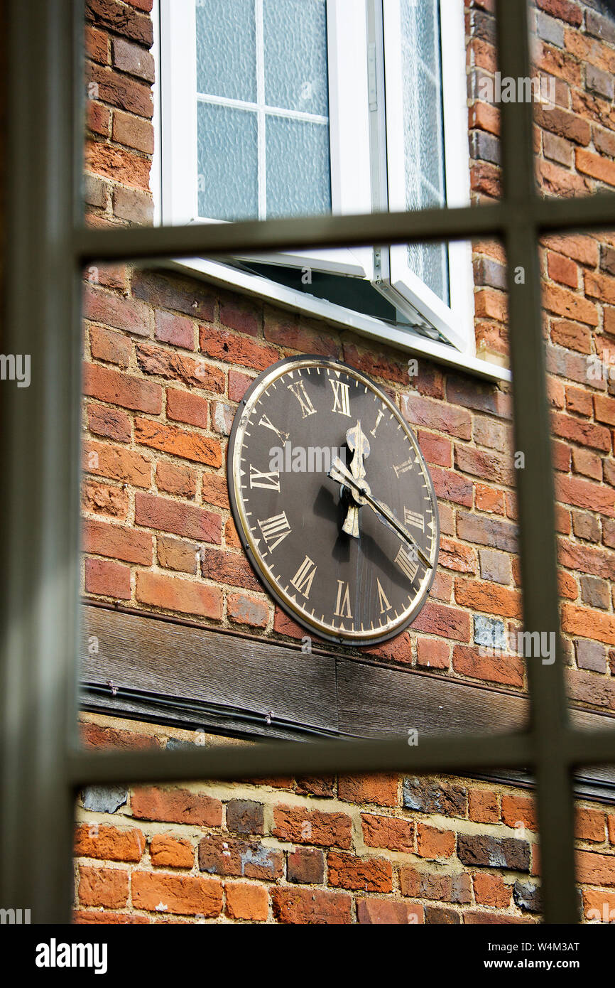 An old clock on the wall of an ancient building seen through a casement ...