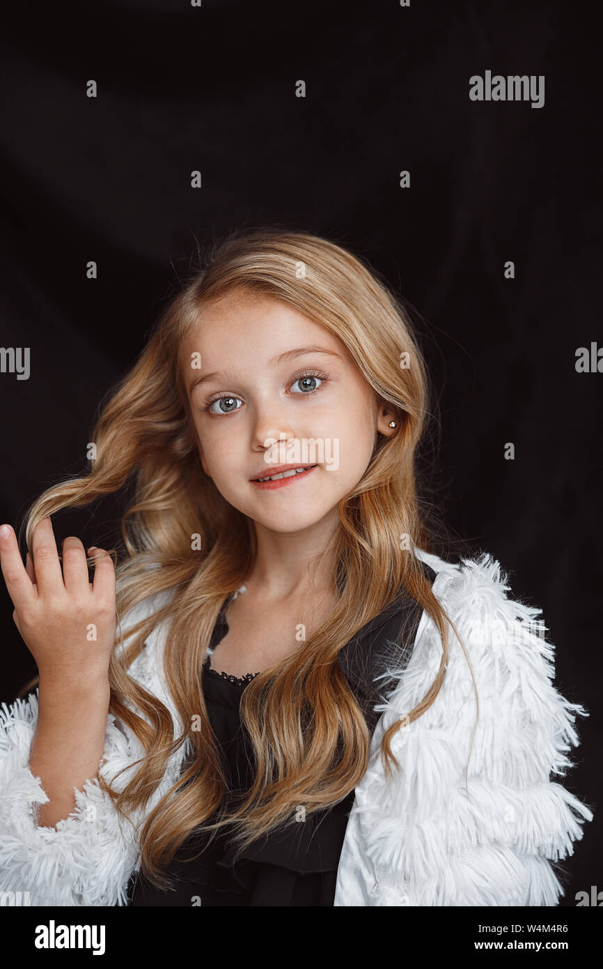 Stylish little smiling girl posing in white outfit isolated on black ...