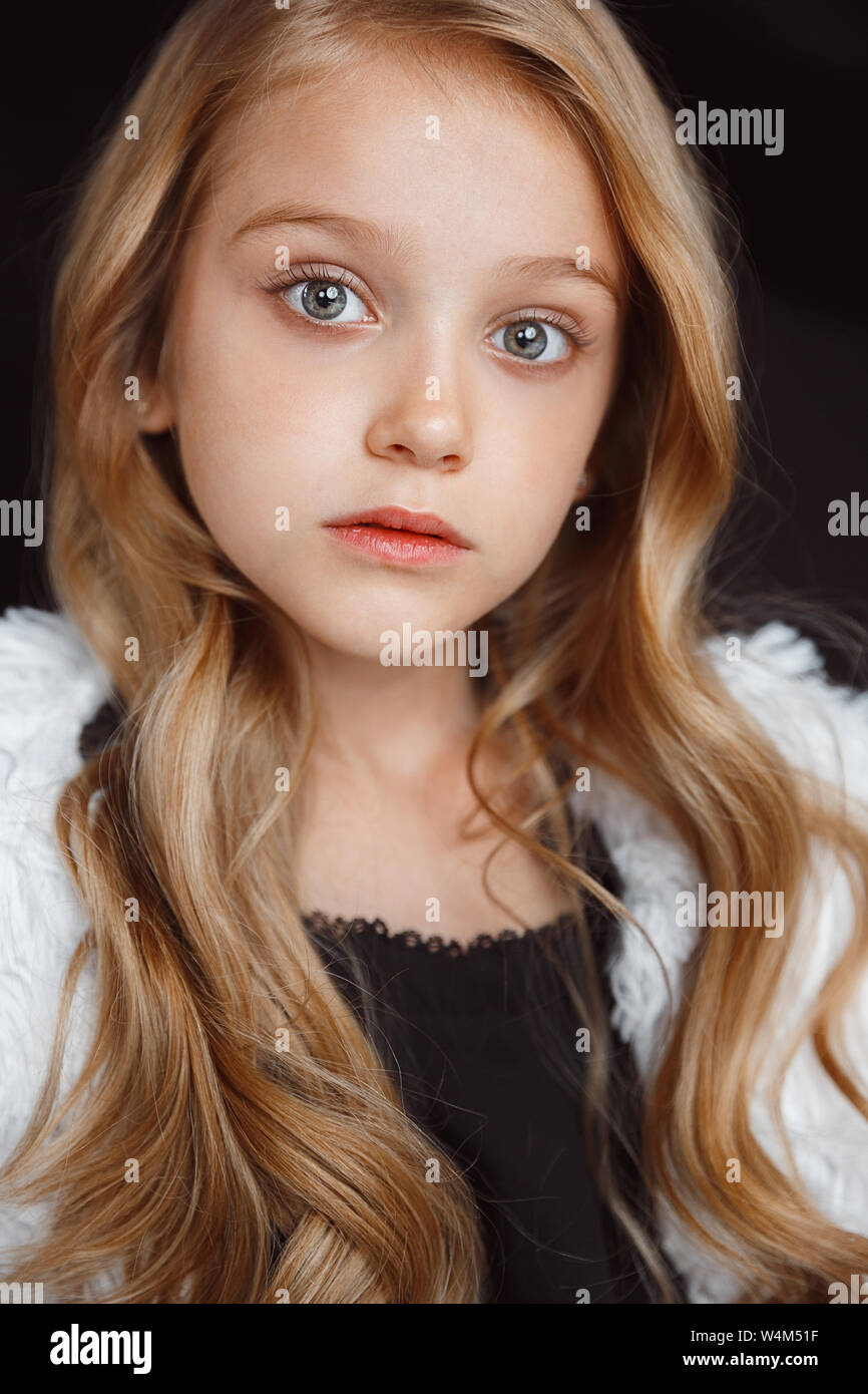 Stylish little smiling girl posing in white outfit isolated on black ...