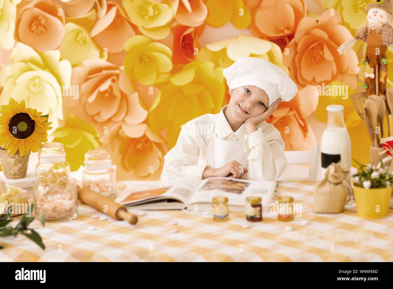 cute little baby prepares delicious dishes in the kitchen on a floral ...