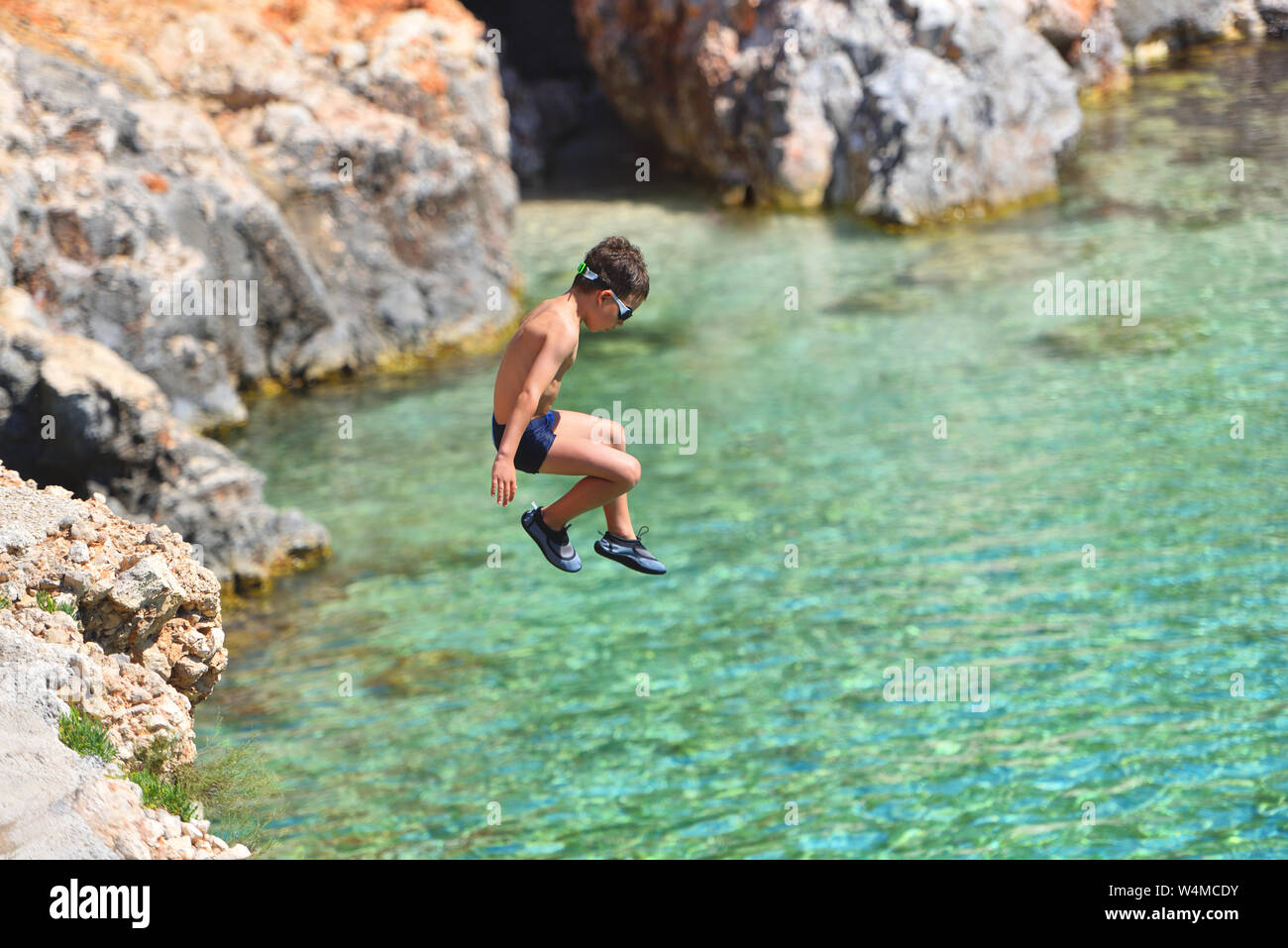Little boy jumping off cliff into the ocean. Summer fun lifestyle ...