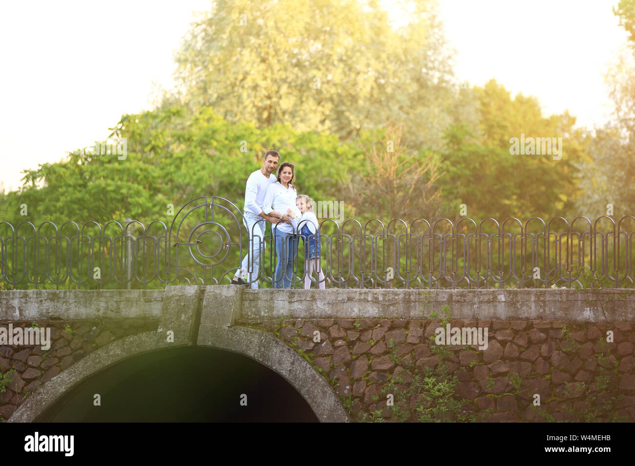Pregnant woman with her daughter and husband in a park on a bridge on a ...