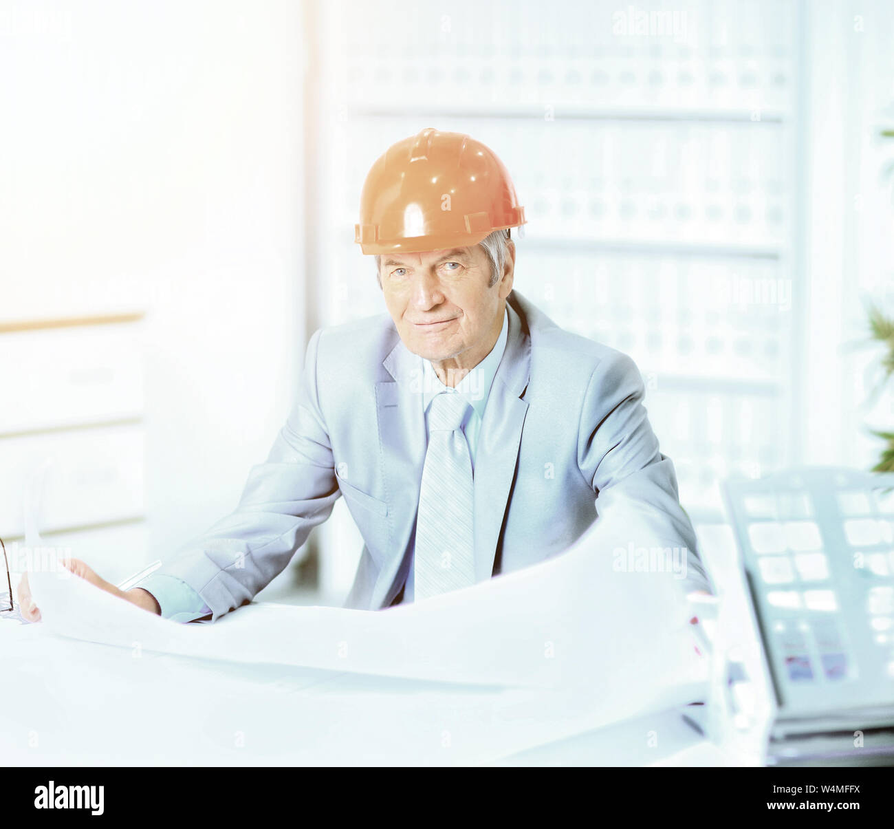 Portrait of professional architect with blueprints sitting behind table ...