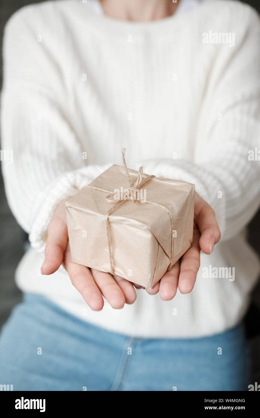 Woman in white knitted sweater giving wrapped gift. Close up Female ...
