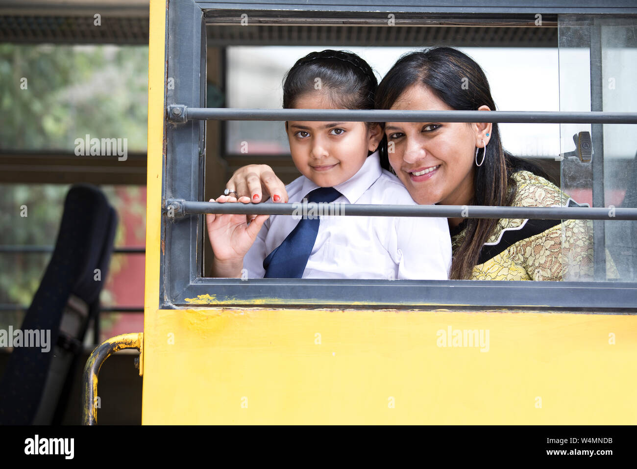 Happy teacher and schoolgirl looking out through window of school bus ...