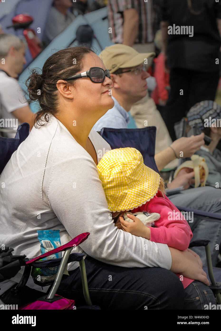 A woman and her small daughter sitting in a crowd together enjoying an ...