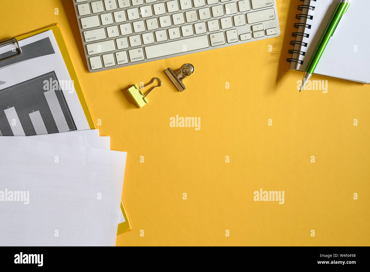 Yellow color office desk, top view with keyboard, clipboard with paper ...