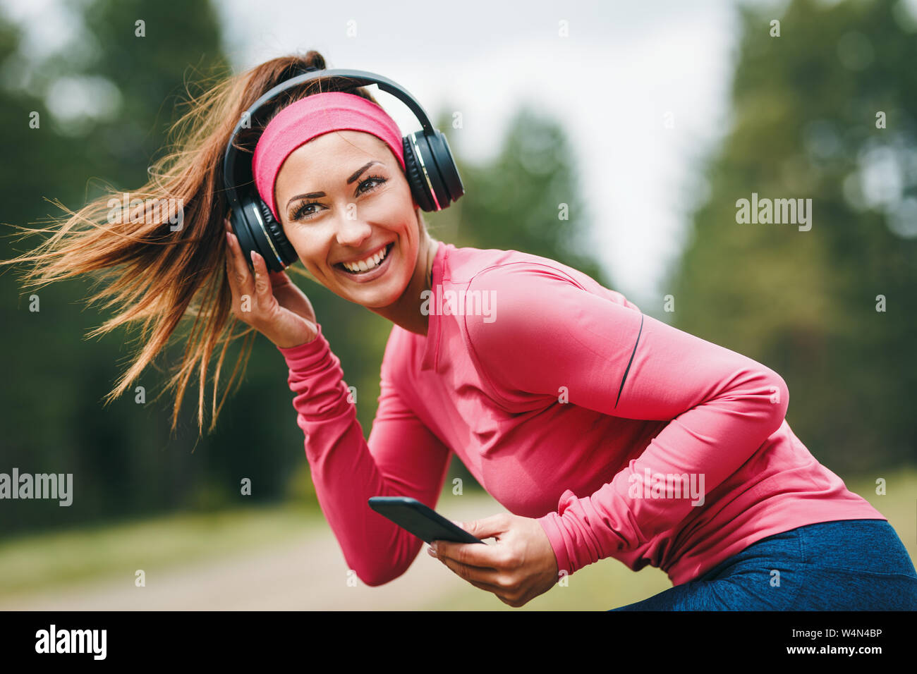 Young cute happy female runner warming up before jogging at morning in ...