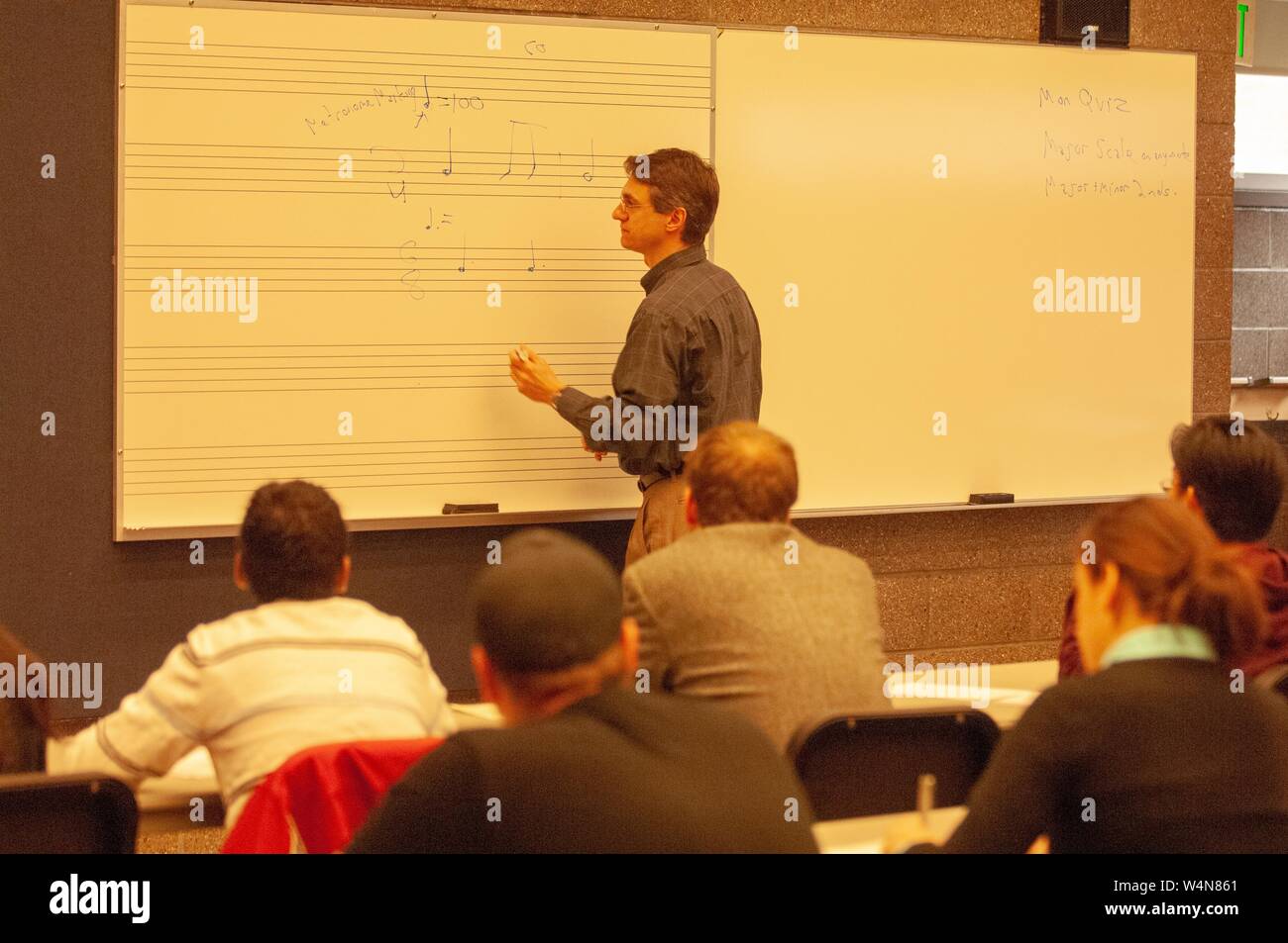 Students watch an instructor write musical notations on a whiteboard ...