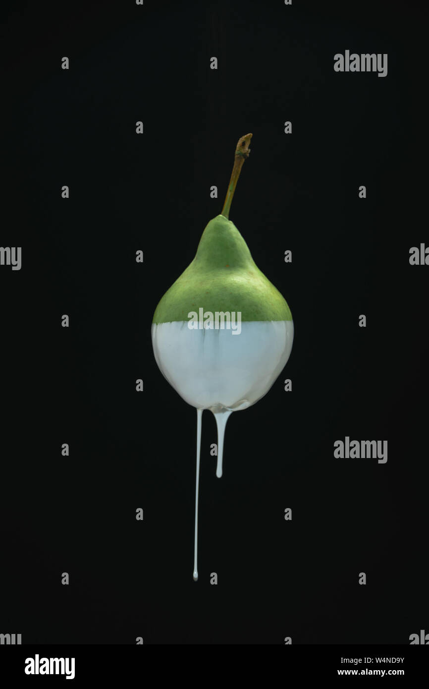 Green Pear dripping white paint on a black background Stock Photo - Alamy