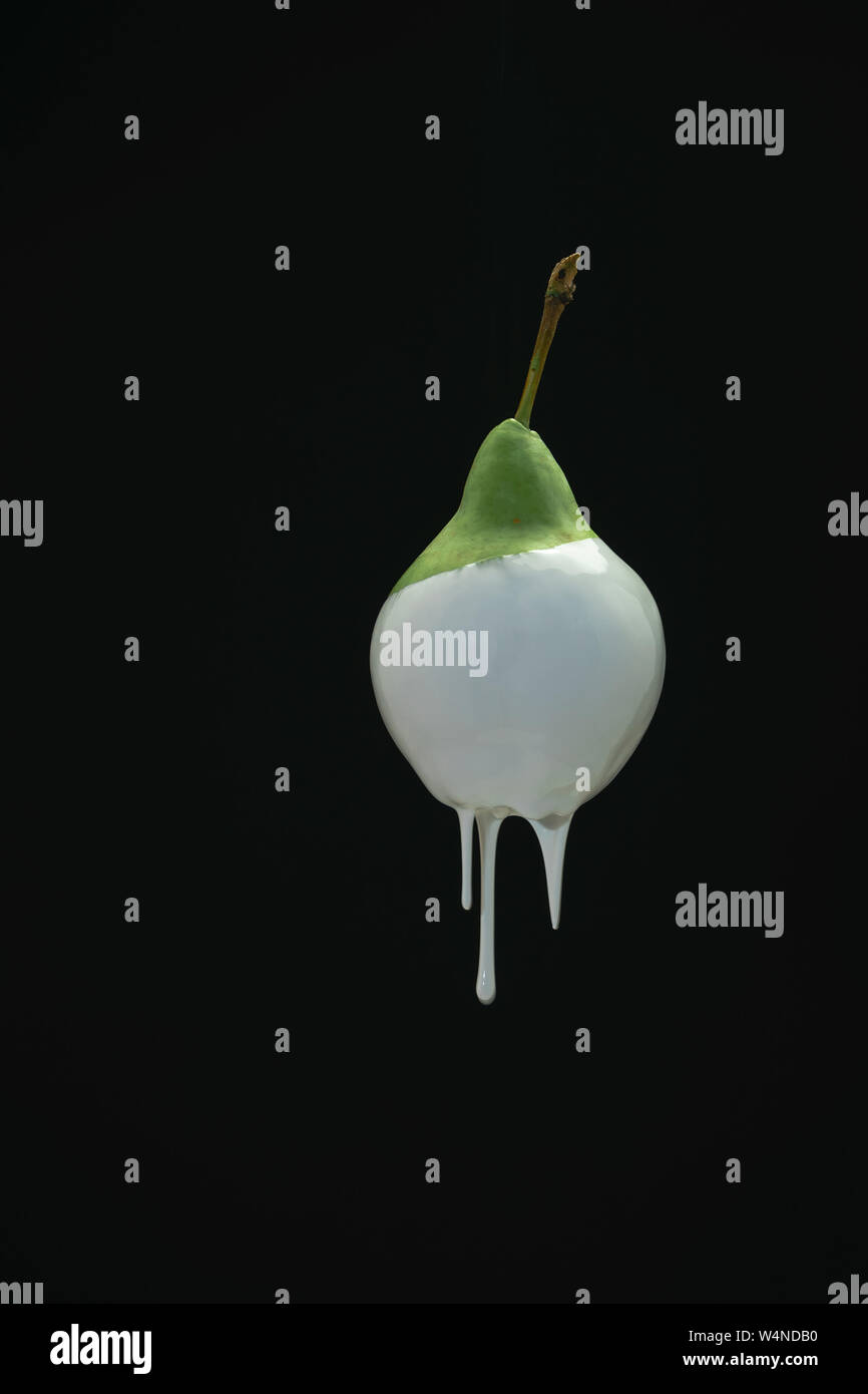 Green Pear dripping white paint on a black background Stock Photo - Alamy
